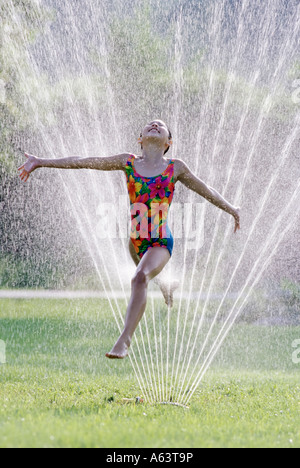 Girl jumping through lawn sprinkler Stock Photo - Alamy