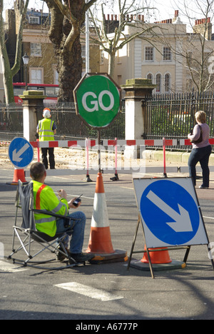 Workman with a stop and go sign controlling traffic at roadworks in ...