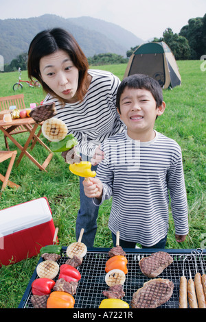 Mother standing by barbeque grill holding tongs with daughters (8-9) in ...
