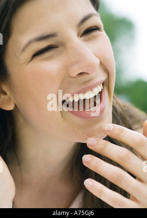 Young woman sniggering or giggling into her hand in a close up cropped ...