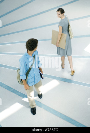 Man and woman walking past each other, both carrying laptop computers ...