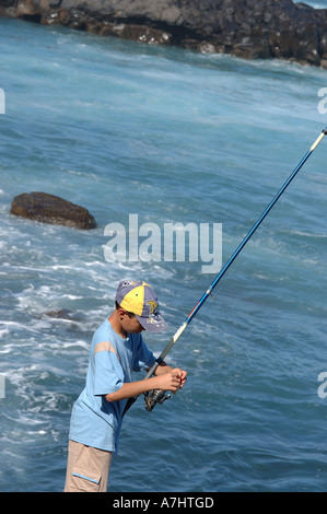 Boy in cap reeling in fishing rod trying to catch a fish with bait ...