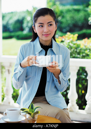young Asian woman holding coffee mug relaxing on sofa smiling at home ...