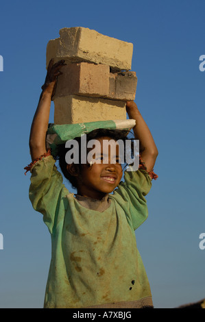 portrait of a boy carrying a stack of bricks on his head which are ...