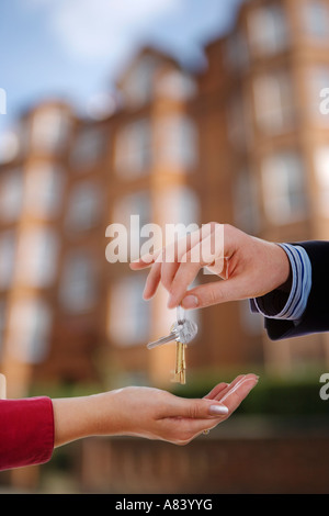 Close up of man's hand passing house keys into woman's hand, house in ...