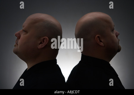 Profile of Caucasian bald identical twin men standing back to back and ...