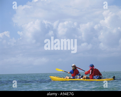 Two people in a kayak paddling on calm blue water, with cliffs in the ...