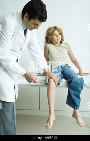 Doctor checking boy's reflexes with reflex hammer, side view, cropped ...