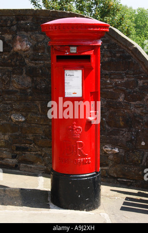 A traditional bright red English post box with a back-drop of an ...