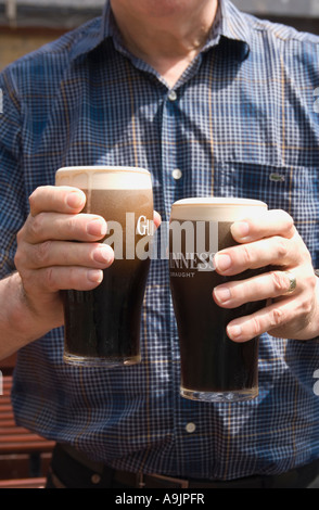 Man holding two pints of stout in plastic pint glasses Stock Photo - Alamy
