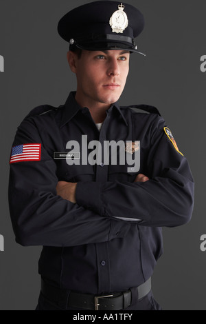A strong looking police officer with his arms folded and his patrol car ...