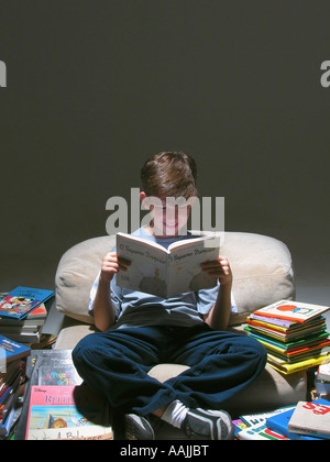 Boy (6-7) surrounded by stacked books, reading one, portrait Stock ...