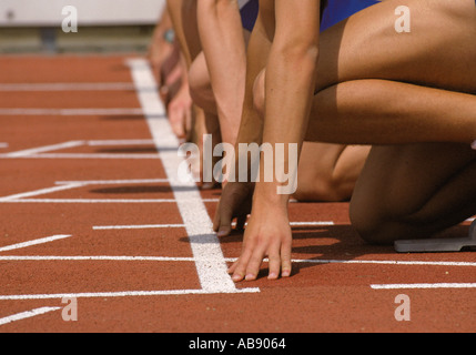 Athlete crouching at the starting line of a running track with gold ...
