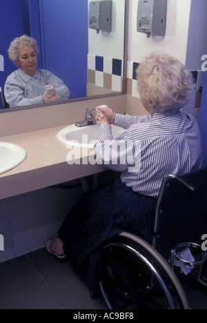 Elderly woman washes her hands with soap under the tap in the bathroom ...