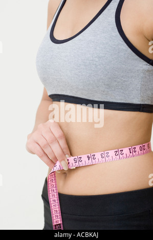 Midsection of woman measuring waist while standing against gray ...