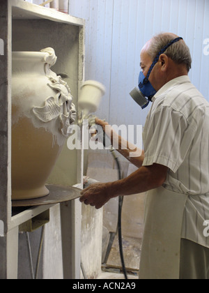 Man spraying glaze on pottery piece in spray booth at a ceramics ...