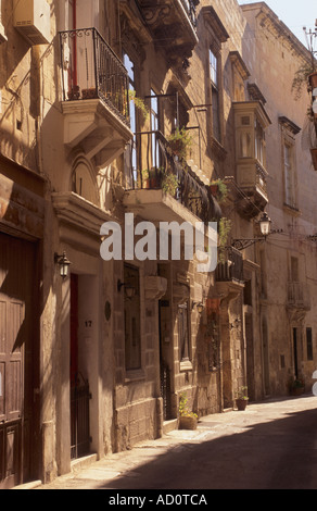 A narrow street in Valletta, Malta, in shadow, with a church dome in ...