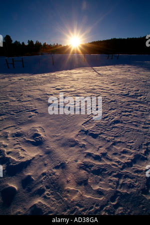 The sun sets over a field covered in snow highlighting the undulating ...