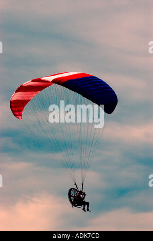Powered parachute ultra light aircraft flying by in blue sky with pilot ...