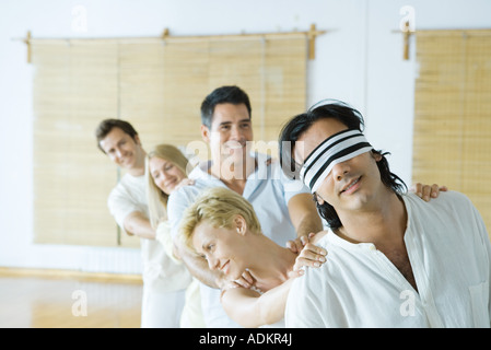 Group of adults standing single file holding onto each others ...