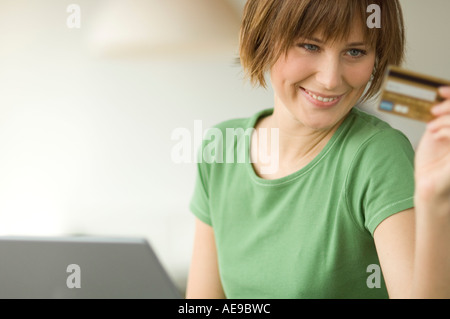 Young woman smiling, holding a credit card and smartphone for online ...