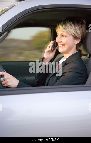 Woman driving and smiling while talking on a mobile phone in a car ...