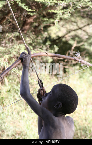 Young tribal boy with bow and arrow walking over dry woods along with ...