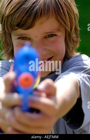 cheerful boy holding toy gun while standing with hands on hips and ...
