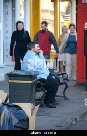 A big fat obese man sat down eating food outside in the high street in ...
