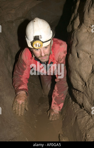 a male caver crawls through a tight constricted muddy passageway in the ...