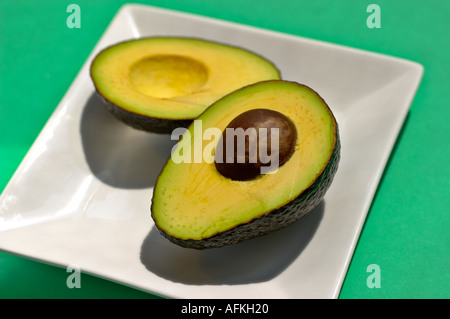 Postcard-style graphic shot of a sliced avocado on white square plate ...