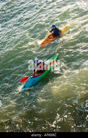 Two people in a kayak paddling on calm blue water, with cliffs in the ...