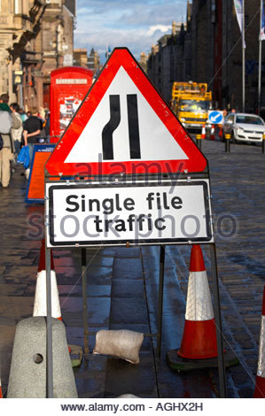 A triangular roadworks sign and traffic cone at the side of a road at ...
