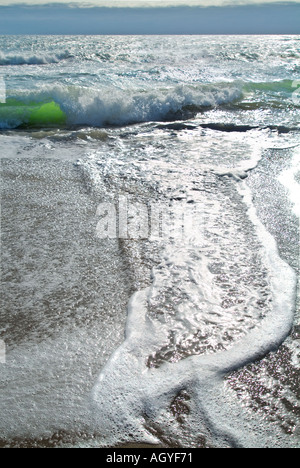 A close up as the foamy sea surf washes up over a people beach on the ...