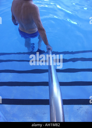 Hand rail going down into swimming pool with chairs and a fence in the ...