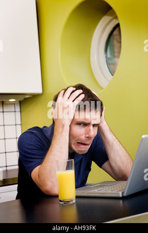 A worried computer user sits in his kitchen with a desperate look on ...