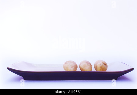 Three neat and clean potatoes on the end of a rectangular plate against ...