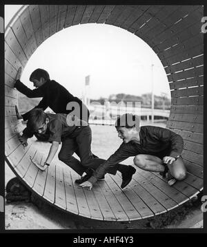 Three boys trying to maintain their footing on a rotating barrel or ...