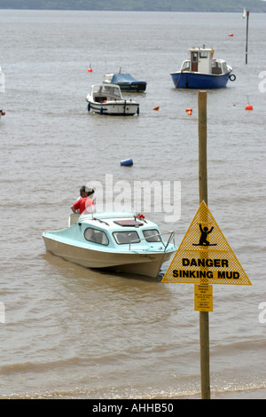 A sign warning of sinking mud showing a man up to his knees in mud and ...