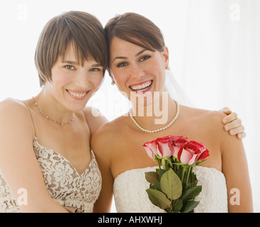 Portrait of happy bride and bridesmaid with bouquet standing in bedroom ...