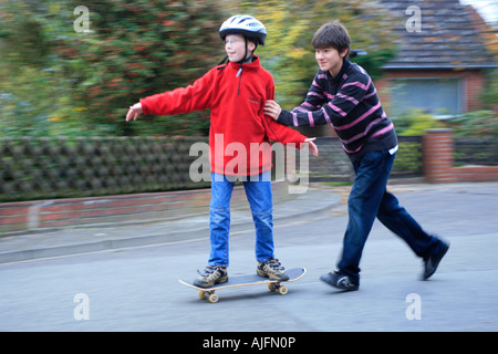 boy pushing friend on skateboard Stock Photo - Alamy