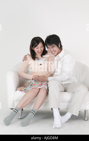Young Asian woman with pregnancy test sitting on toilet bowl against ...