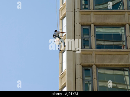 Looking up a t a window washer dangling from a rope on the side of a ...