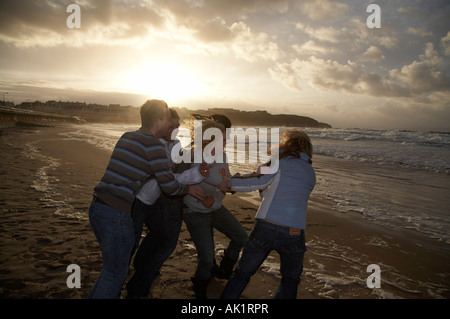group of teenage student friends messing about on a beach at sunset ...