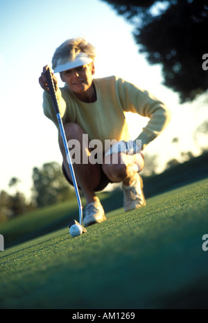 Woman playing golf lining up a putt on the green with her golf cart and ...