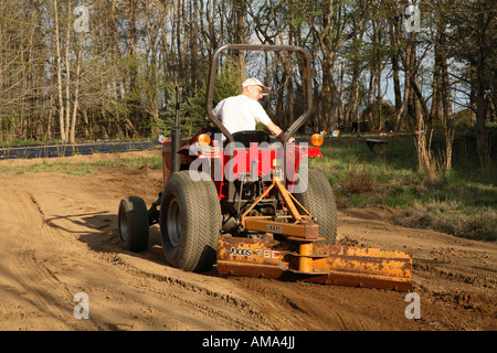 Man driving small tractor and scraping field with grading blade Stock ...