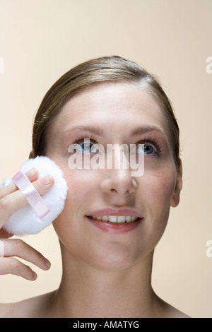 Portrait of a young woman with powder puff on her cheek, indoors ...