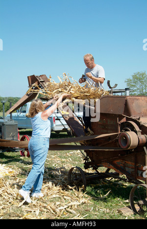 Husband and wife farmers thrash corn in a antique threshing machine ...