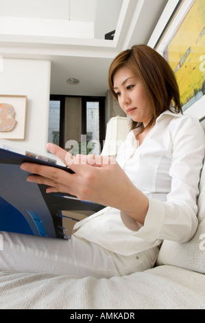 Asian woman reading book while relaxing comfortably on modern couch at ...