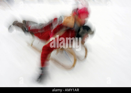 Parent riding a kid on a sled, moving fast on the bumpy snow track ...